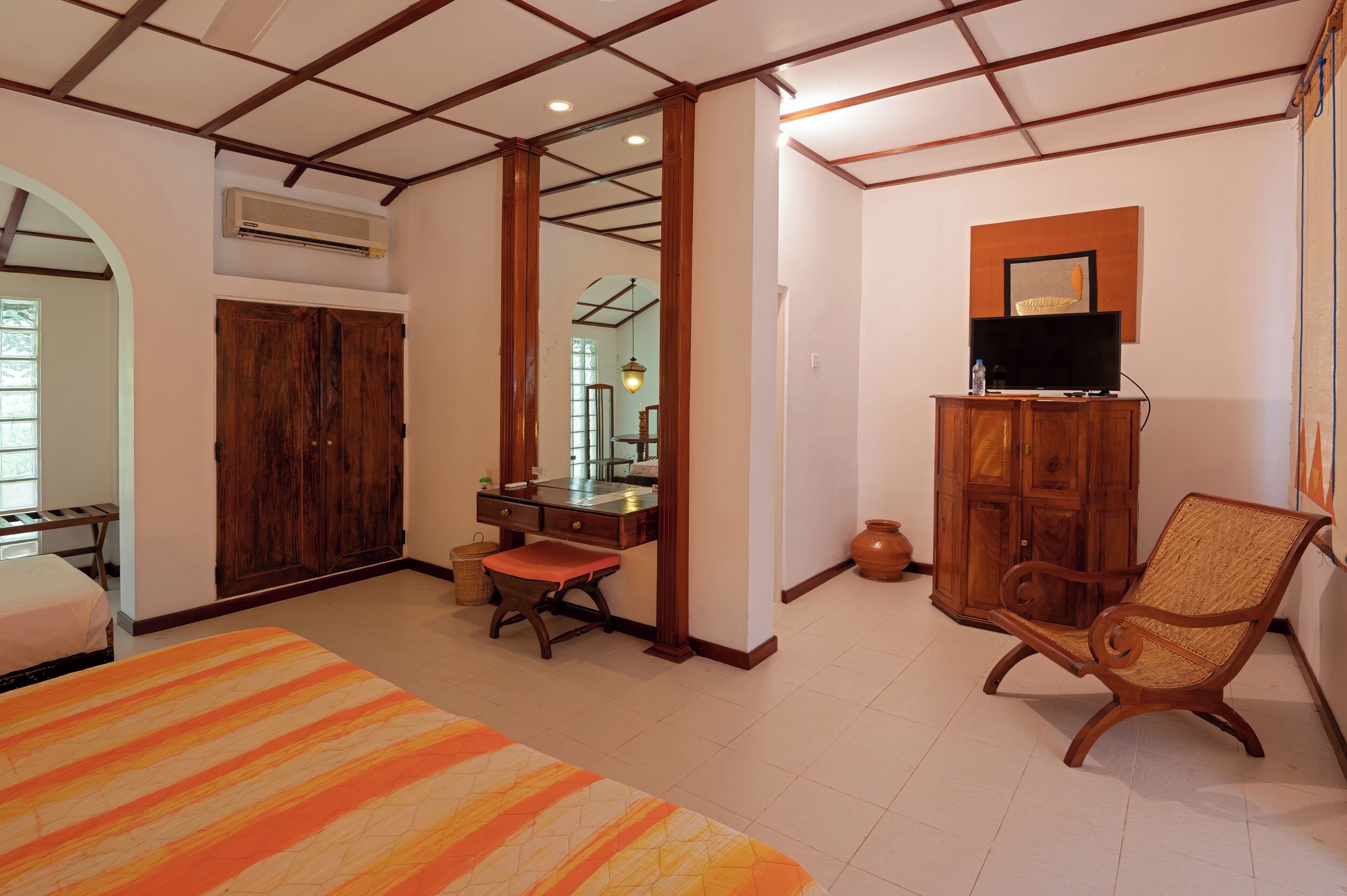 Quarto de hotel com cama, escrivaninha, cadeira, televisão e guarda-roupa.