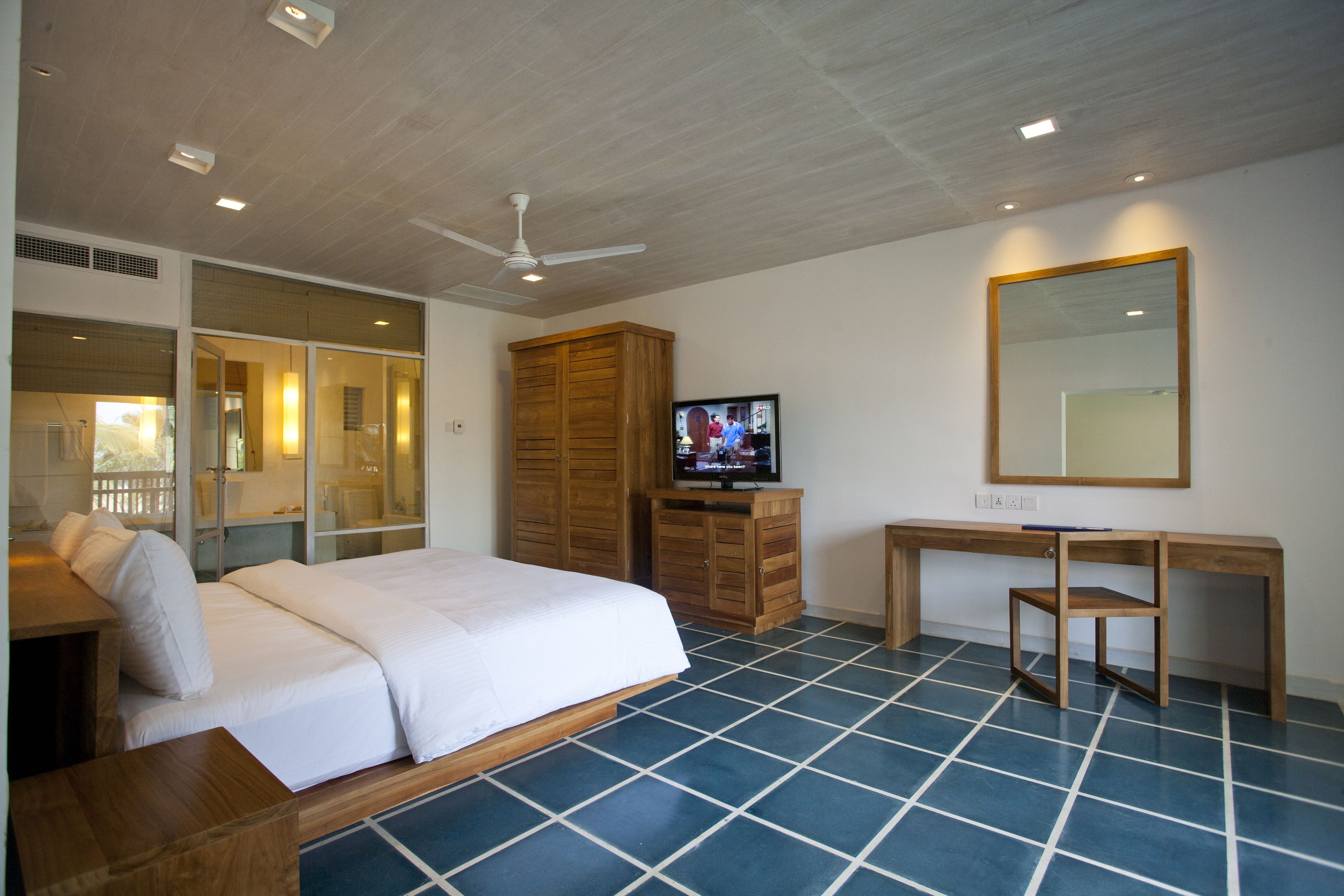 Quarto de hotel com cama, guarda-roupa de madeira, televisão, secretária e espelho.