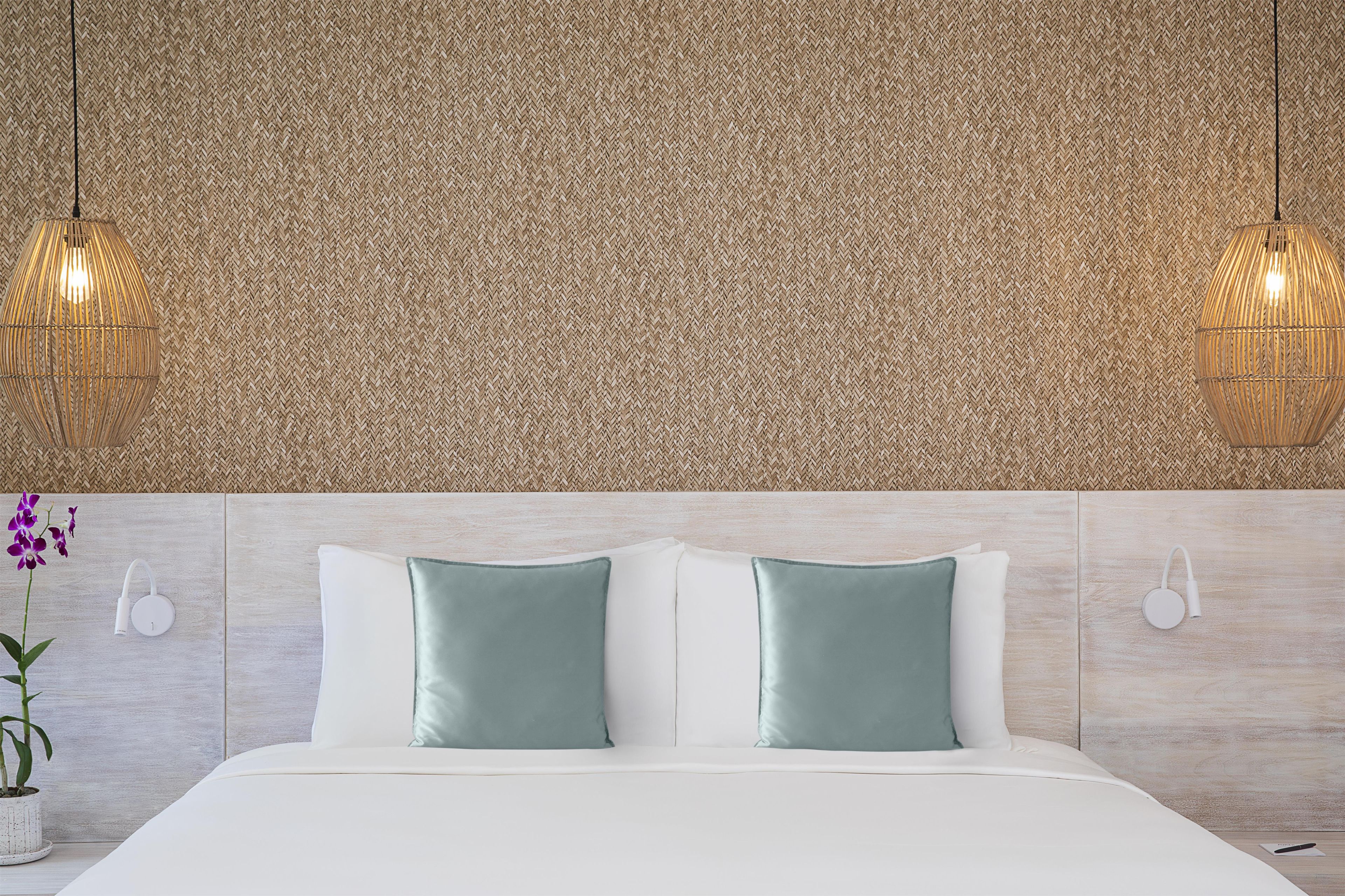 Uma cama com duas almofadas, uma parede com textura e dois candeeiros suspensos.