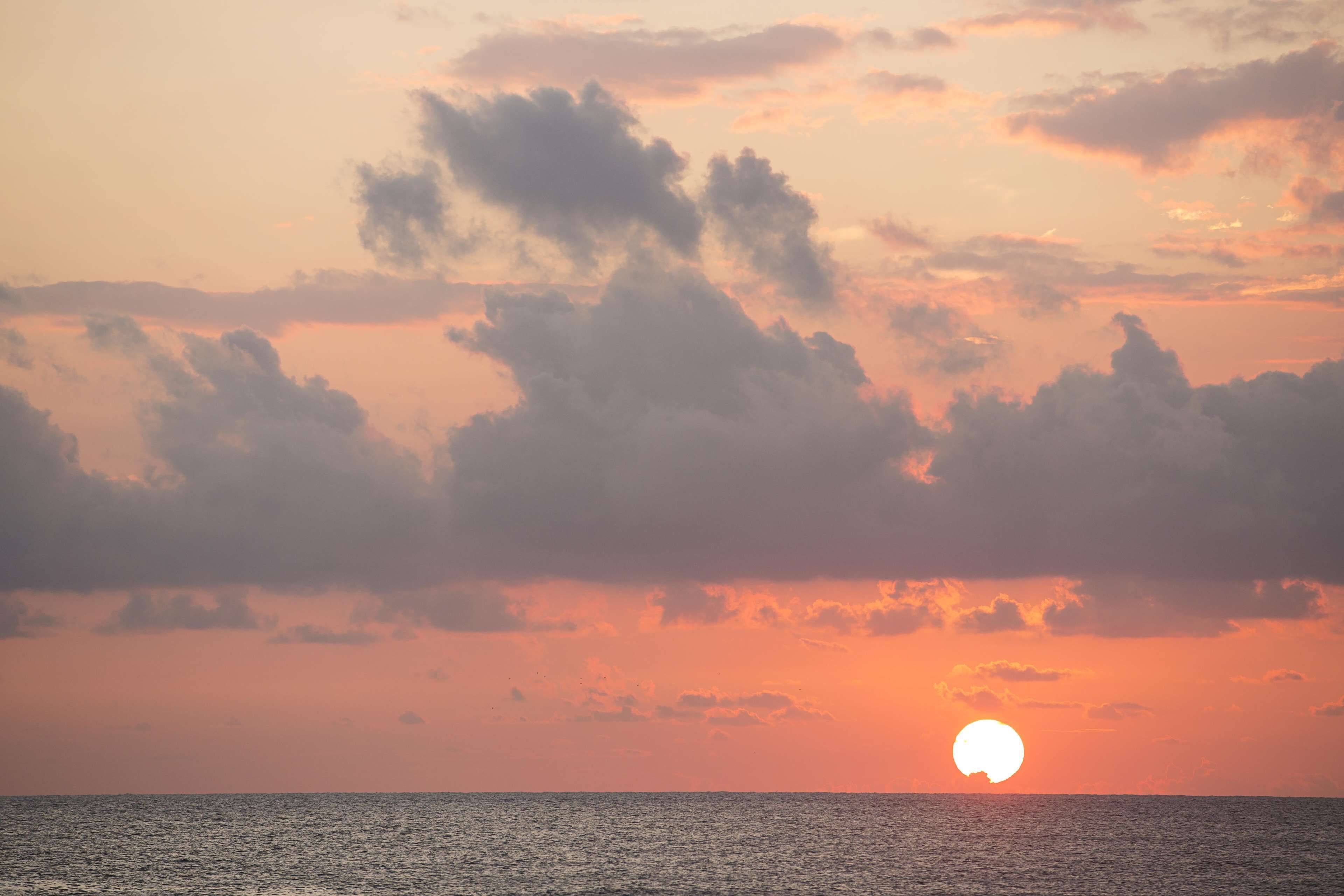 Um pôr do sol sobre o oceano, com nuvens no céu.