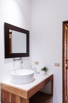 Casa de banho com lavatório branco, espelho com moldura escura e toucador de madeira.