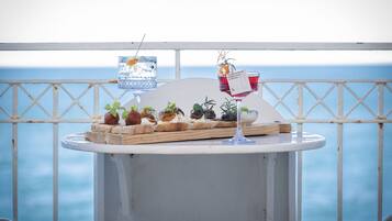 Uma mesa com comida e bebidas numa varanda com vista para o mar.