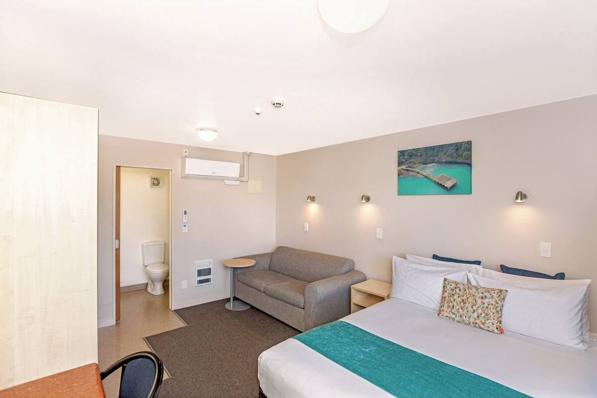 Quarto de hotel com cama, sofá, uma mesinha e um quadro na parede.