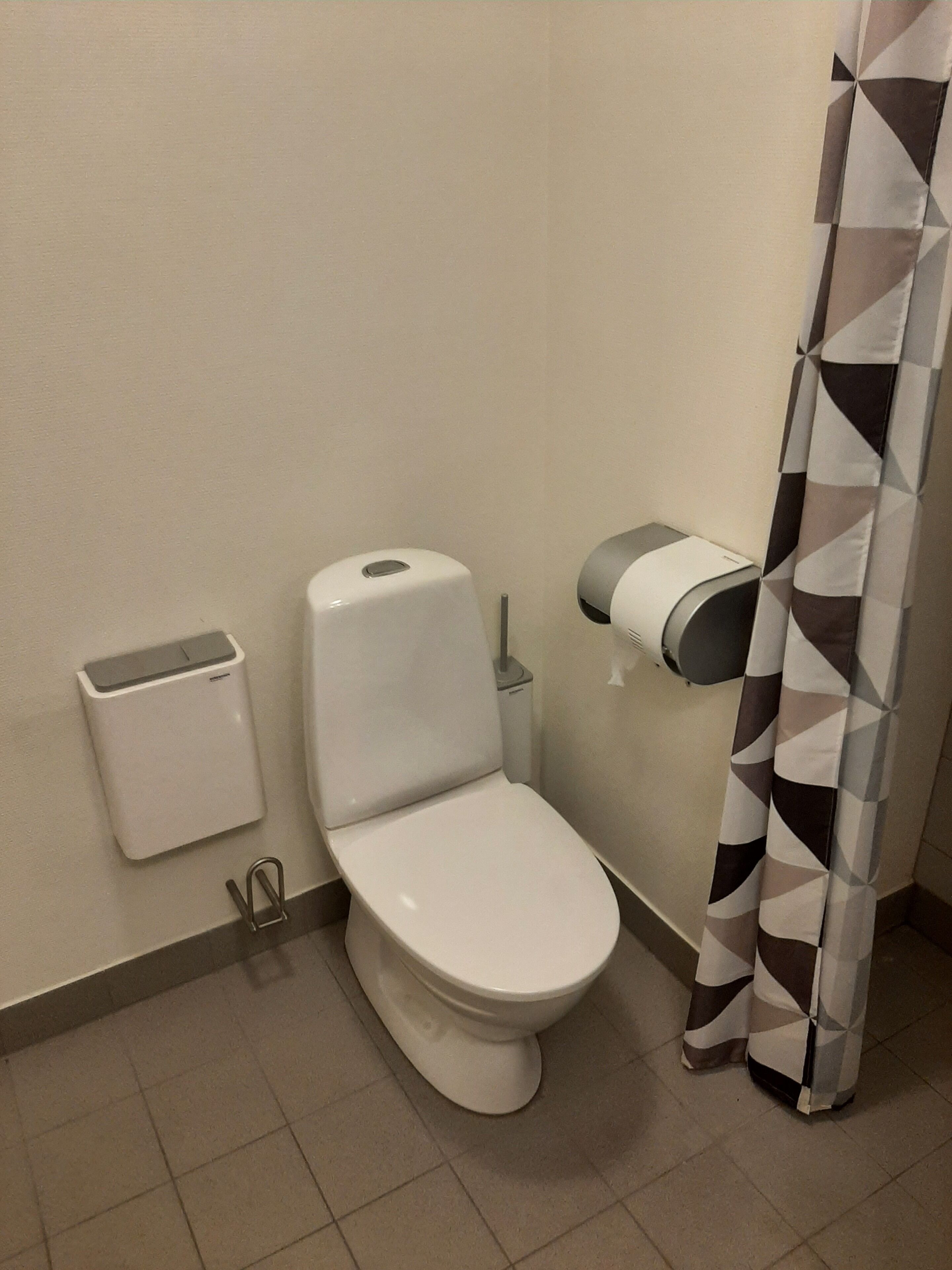 Um banheiro padrão com vaso sanitário, lixeira e dispensador de toalhas de papel.