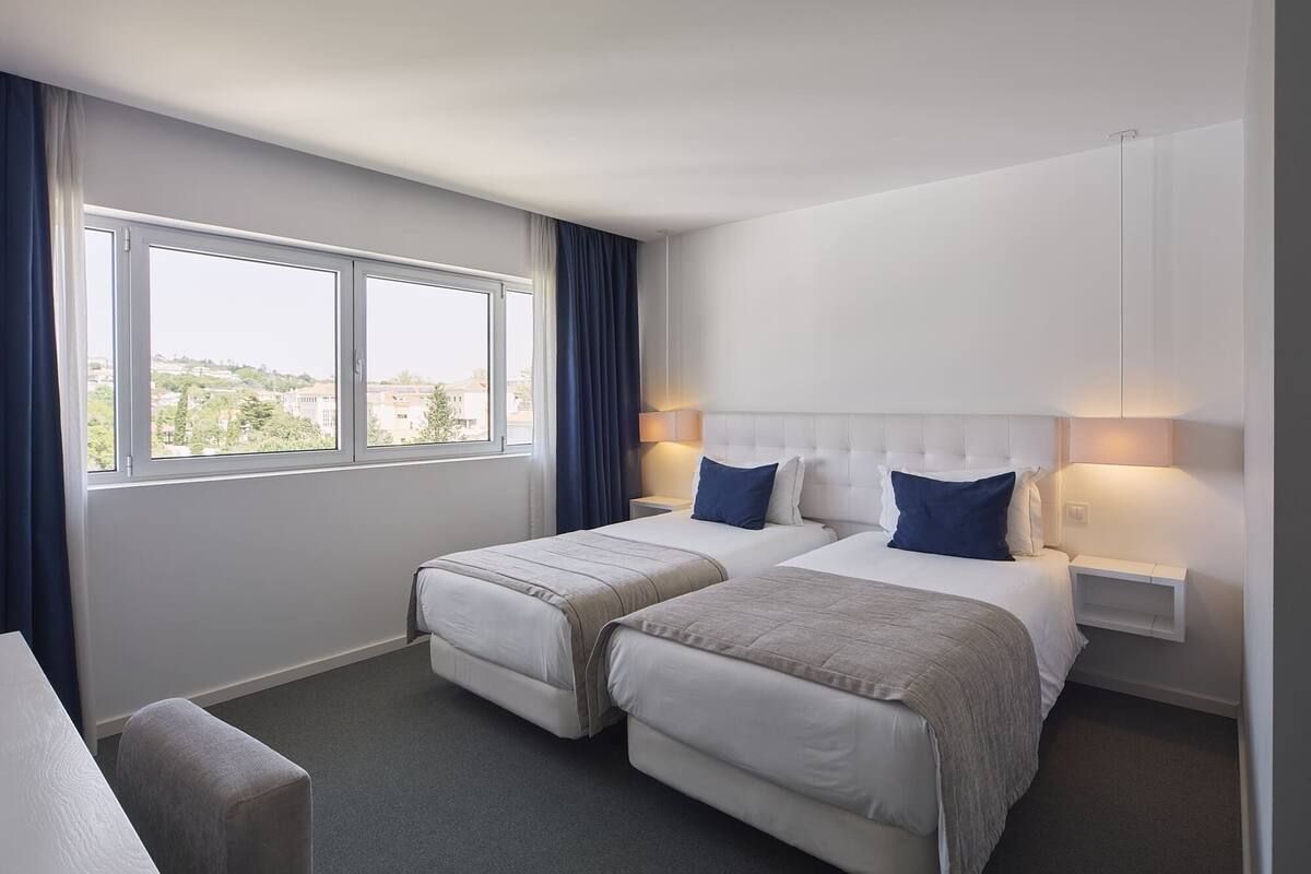 Quarto de hotel com duas camas, vista para a cidade e uma secretária.