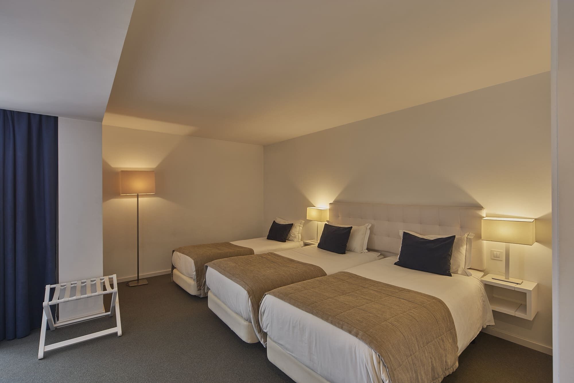 Quarto de hotel com duas camas, abajures, uma mesinha e uma cadeira.