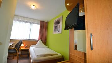 Quarto de hotel com cama, escrivaninha, cadeira, televisão e janela com cortinas.