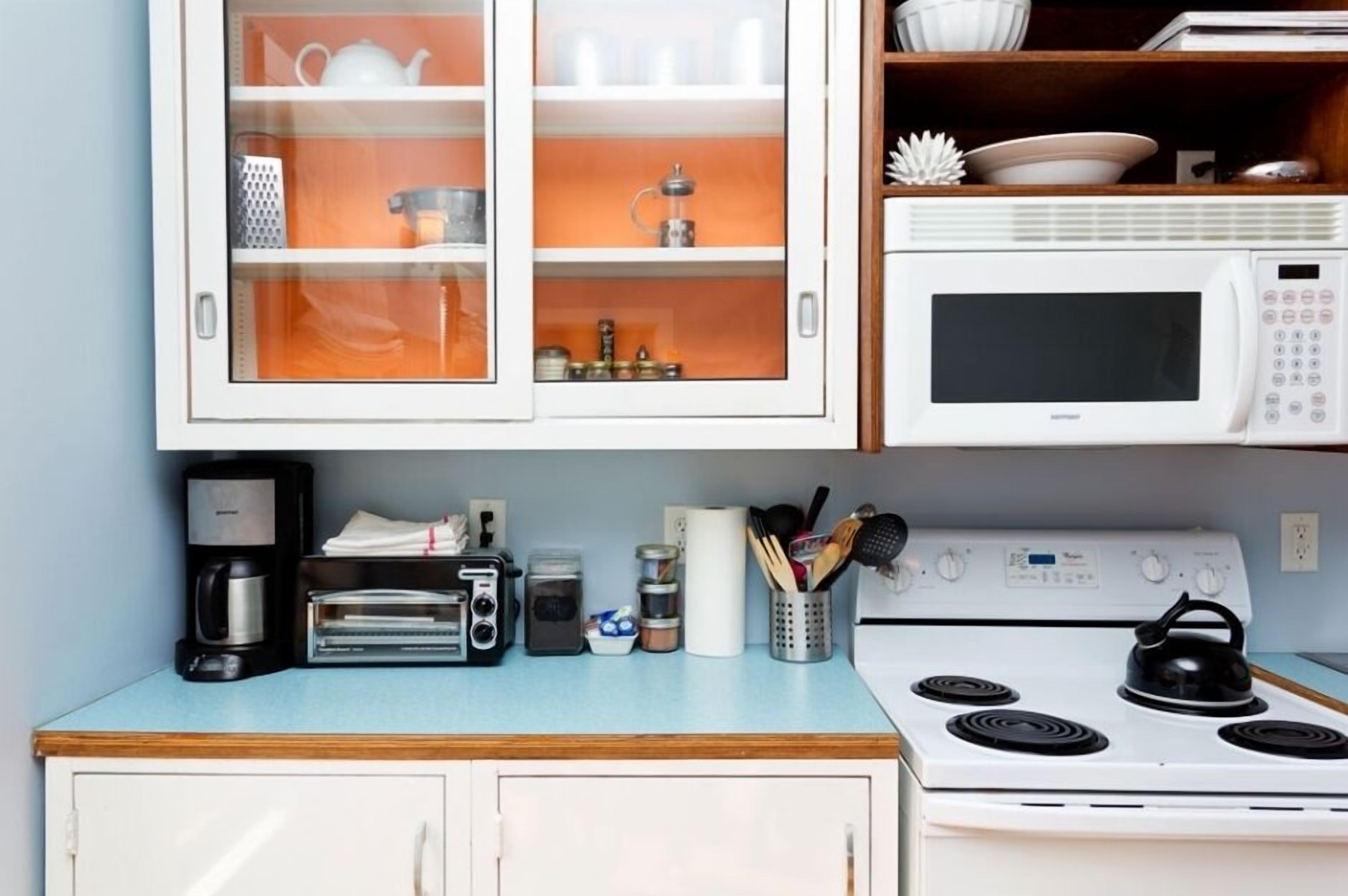 Uma cozinha com fogão branco, micro-ondas e armário com portas de vidro.