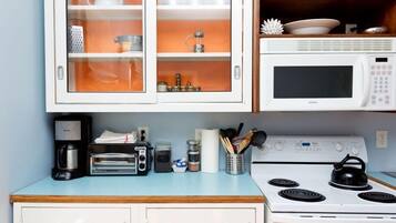 Uma cozinha com fogão branco, micro-ondas e armário com portas de vidro.