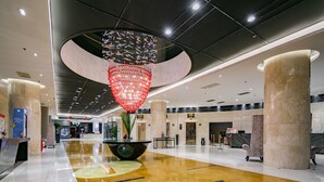 Um hall amplo com um grande candelabro, colunas de mármore e um balcão de recepção.
