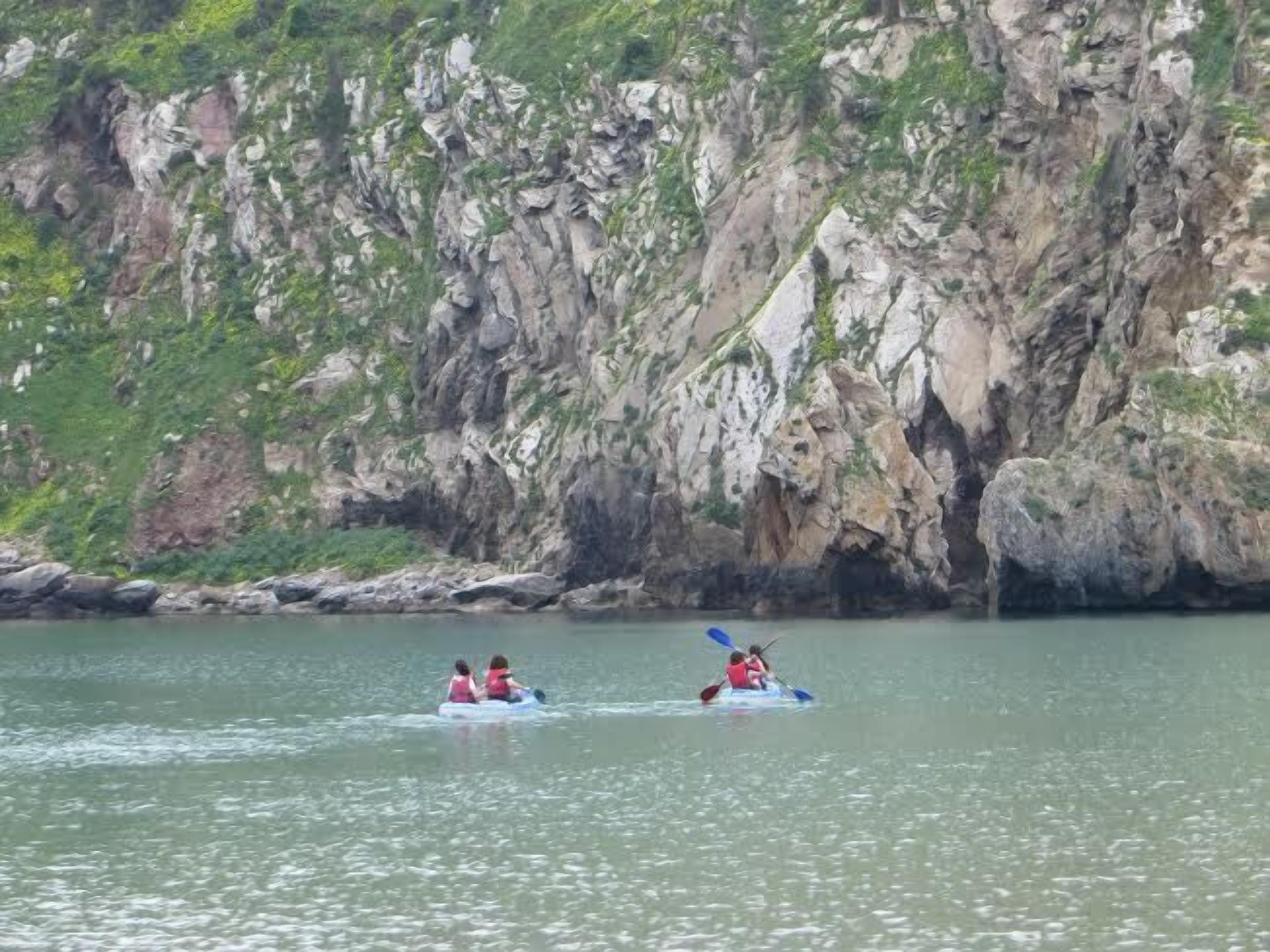 Um caiaqueiro em um rio calmo, com penhascos rochosos ao fundo.