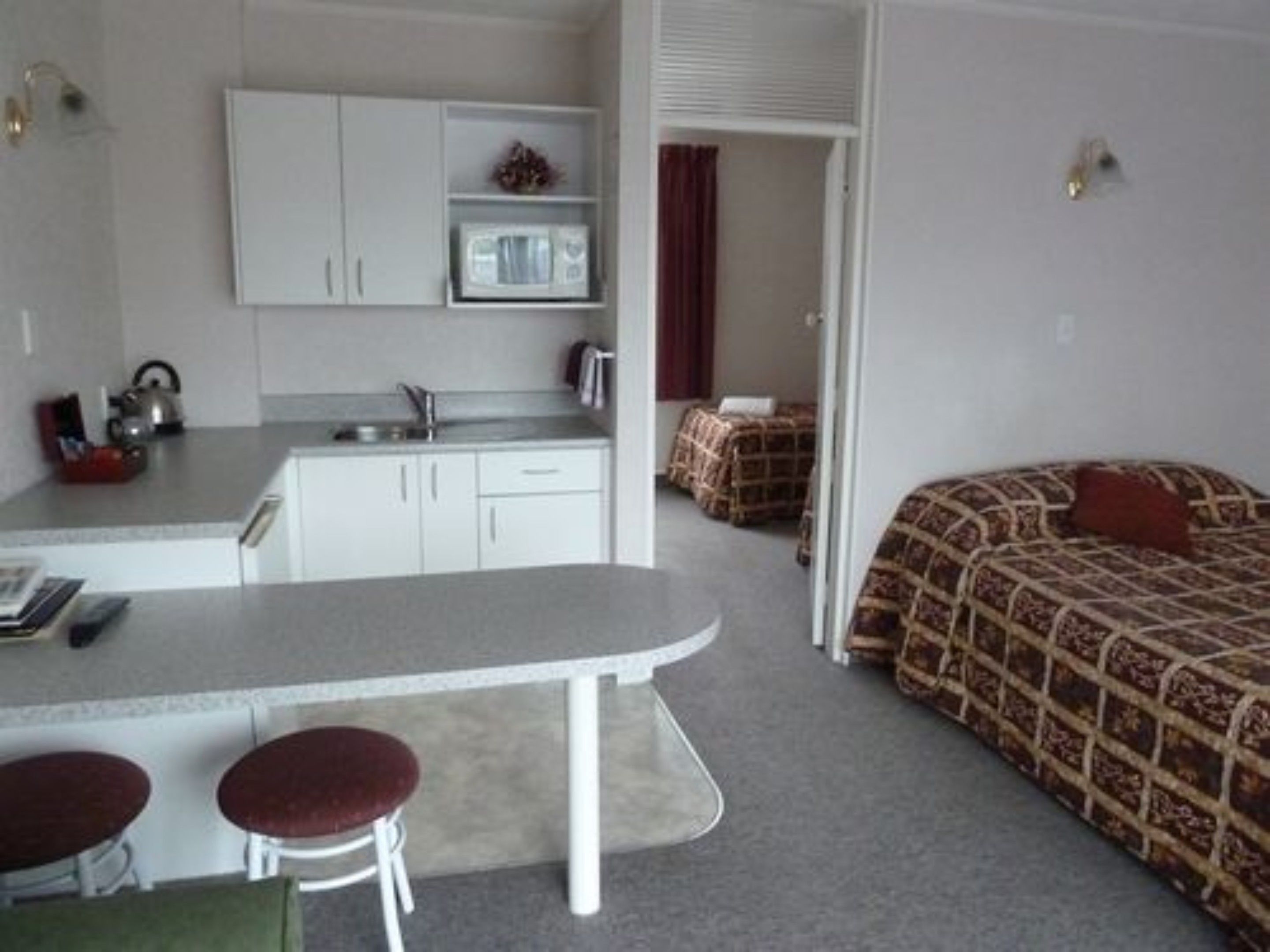 Quarto de hotel compacto com cozinha compacta, cama com roupa de cama estampada e um pequeno espaço de estar com banquetas.