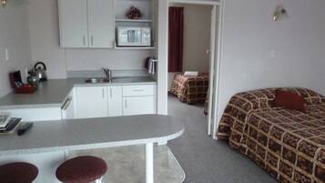 Quarto de hotel compacto com cozinha compacta, cama com roupa de cama estampada e um pequeno espaço de estar com banquetas.