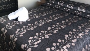 Quarto de hotel com uma cama grande, uma cama menor ao fundo, uma luminária na parede e um quadro na parede.