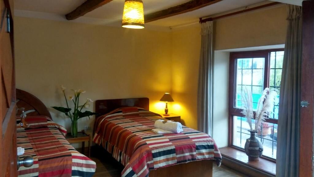 Quarto com duas camas, um abajur, um vaso com penas e uma janela com cortinas.