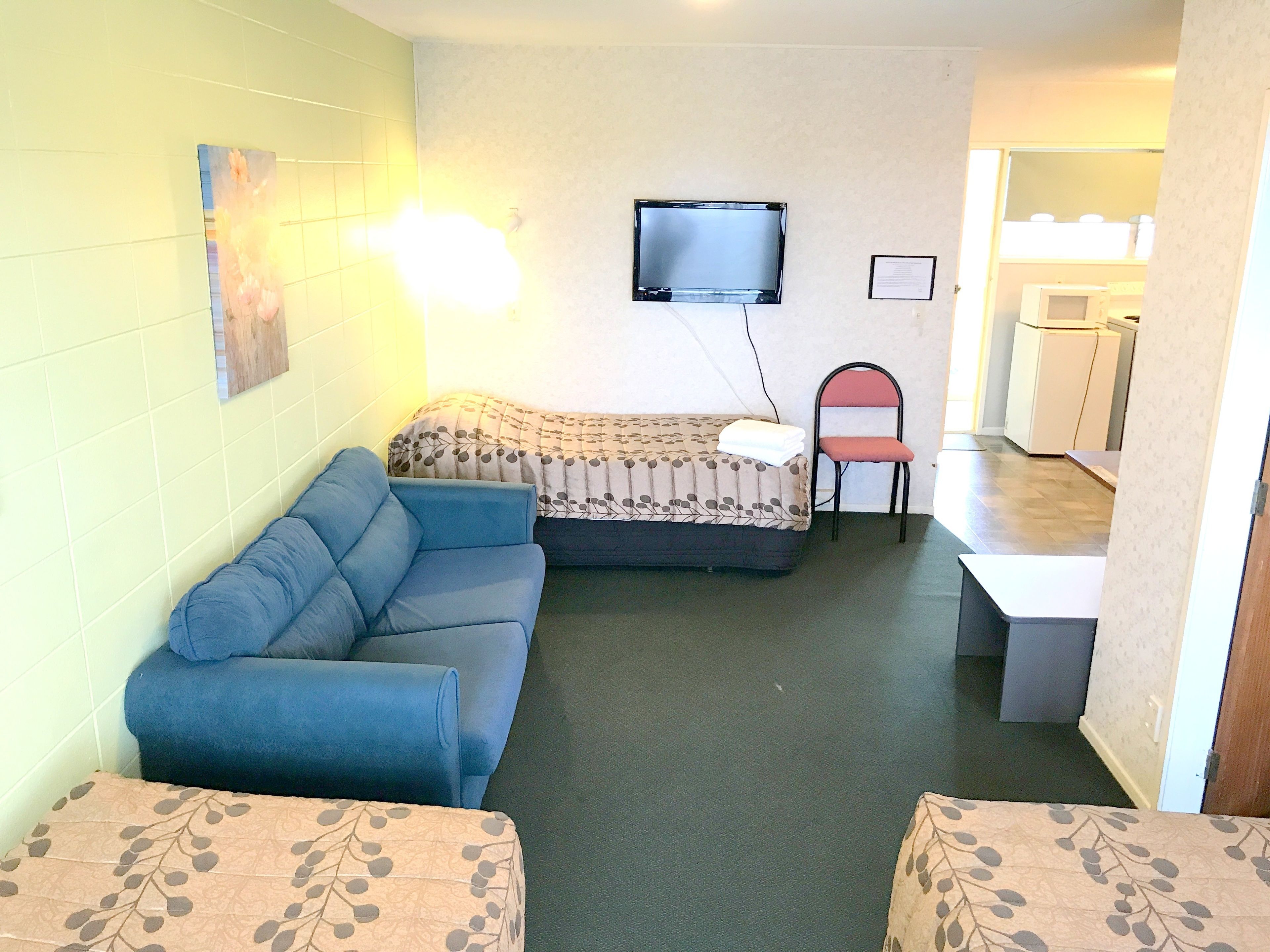 Quarto compacto com sofá, cama, televisão e poltrona.