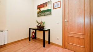 Quarto com porta de madeira, uma mesa pequena com um vaso de flores, um quadro na parede e um aviso proibindo fumar.