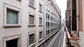 Rua estreita ladeada por edifícios altos com janelas amplas e sacadas.