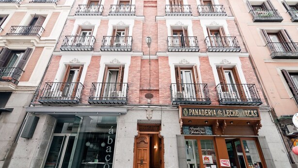 Um edifício de vários andares com uma padaria no andar térreo, apresentando um estilo arquitetônico europeu clássico, com fachadas de tijolos e varandas ornamentadas.