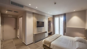 Quarto de hotel moderno com uma cama grande, televisão fixada num painel de madeira, closet espaçoso e casa de banho com sanita e lavatório.