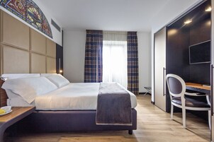 Quarto de hotel moderno com uma cama grande, uma escrivaninha e uma cadeira.