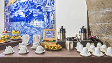 Disposição de buffet de café da manhã com diversos alimentos, estações de chá e café, e uma parede decorativa com azulejos azuis.