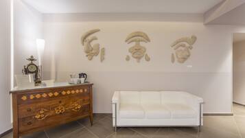 Quarto moderno com sofá branco, aparador de madeira com detalhes entalhados e esculturas nas paredes.