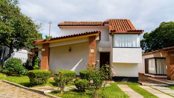 Uma casa de dois andares com telhado de telhas, garagem e um jardim bem cuidado com arbustos e uma roseira.