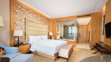Quarto de hotel com uma cama grande, área de estar, escrivaninha e televisão.