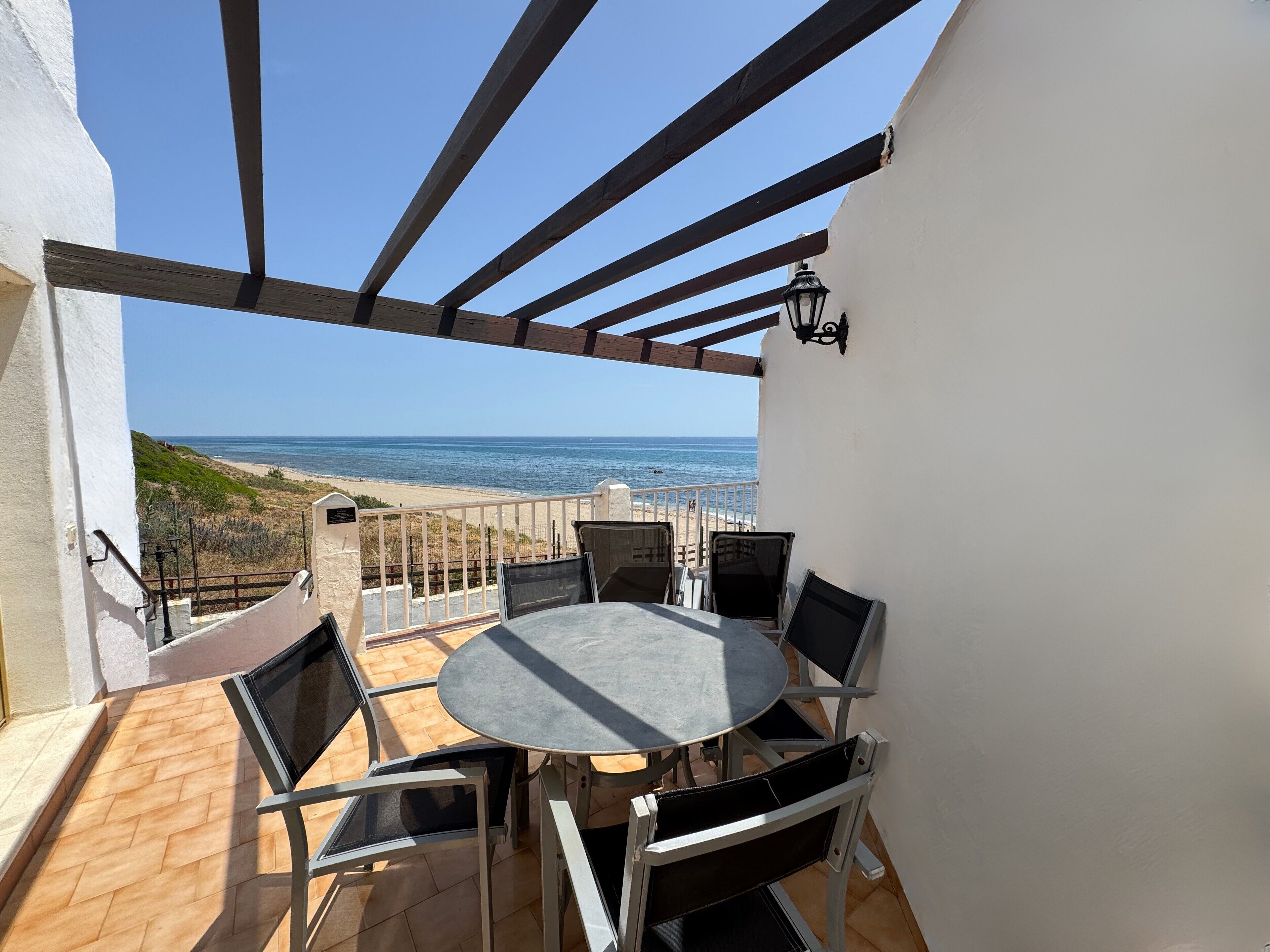 Varanda com mesa redonda e cadeiras, com vista para a praia e o oceano.