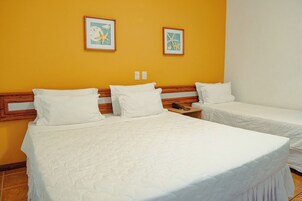 Quarto de hotel com duas camas de solteiro, uma cabeceira de madeira e duas fotografias emolduradas na parede.