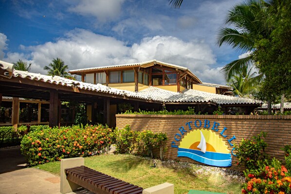 Um hotel com um letreiro temático praiano, um alpendre coberto e paisagismo exuberante.