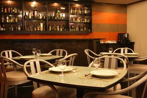 Restaurante com mesas postas, cadeiras e área de bar com prateleiras cheias de garrafas.