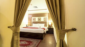 Quarto de hotel com cama, mesa de cabeceira, abajur e tapete vermelho estampado.