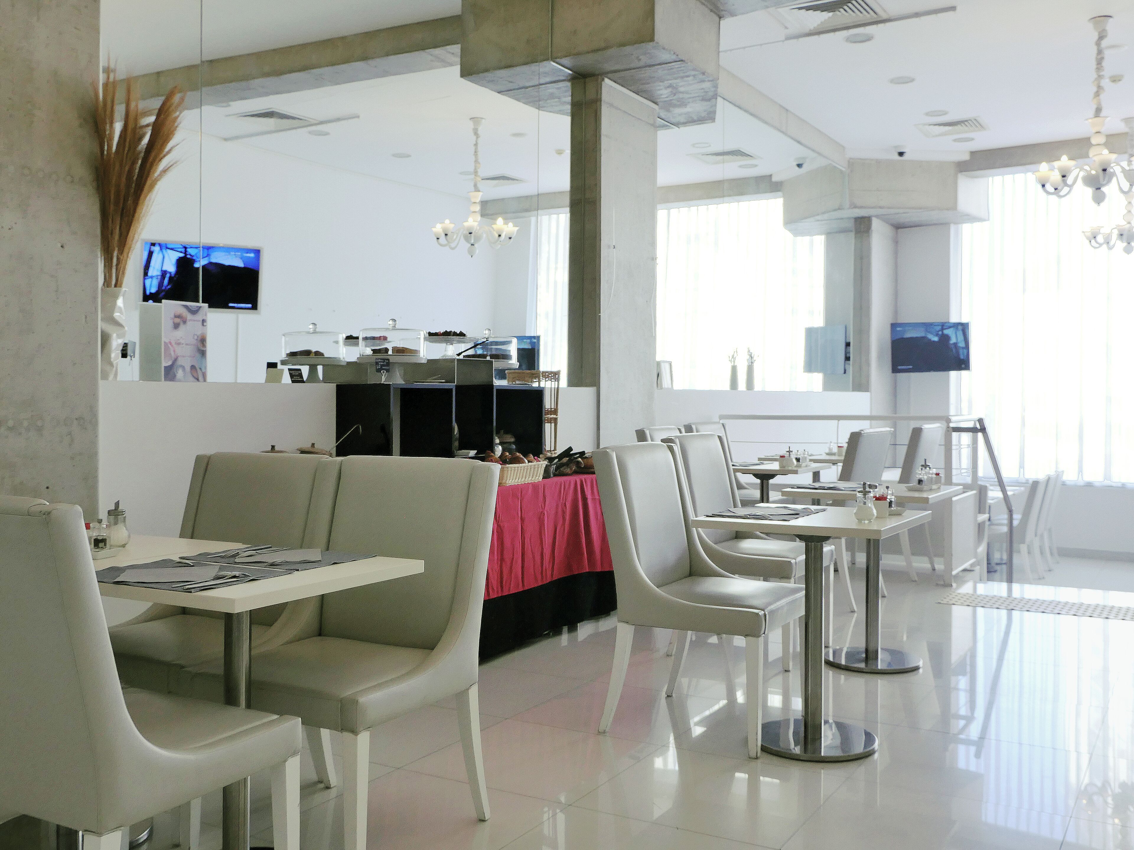 Um restaurante moderno com móveis brancos, toalha de mesa vermelha e uma televisão na parede.