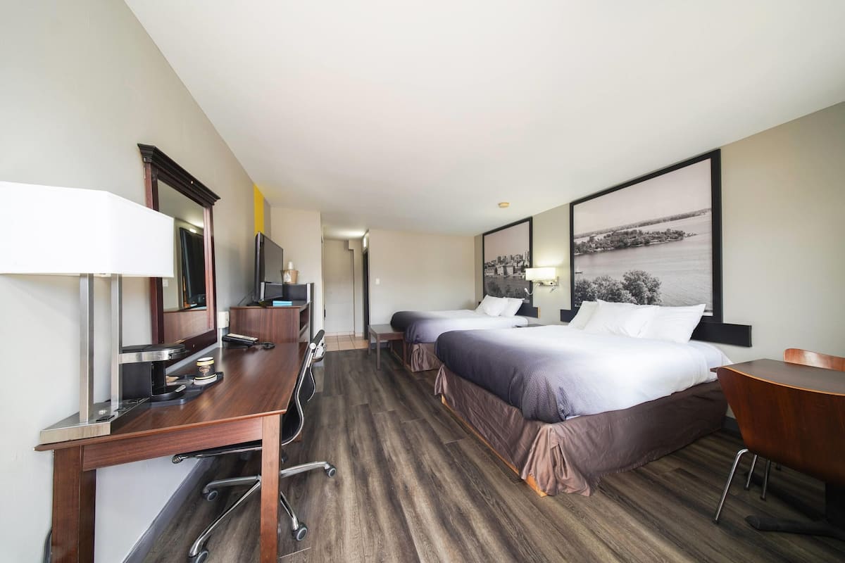 Quarto de hotel com duas camas, uma escrivaninha, uma cadeira, uma televisão e um quadro na parede.