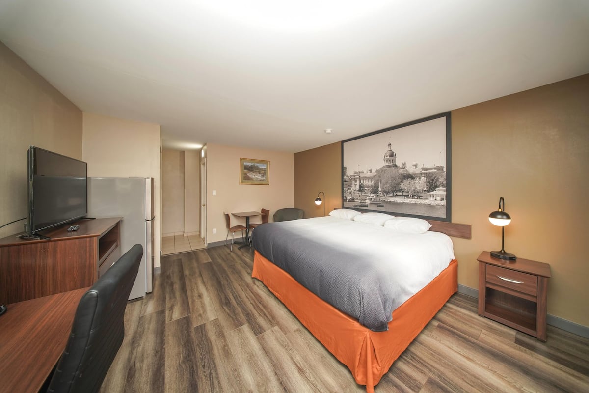 Quarto de hotel com cama, escrivaninha, televisão e pintura da paisagem urbana na parede.
