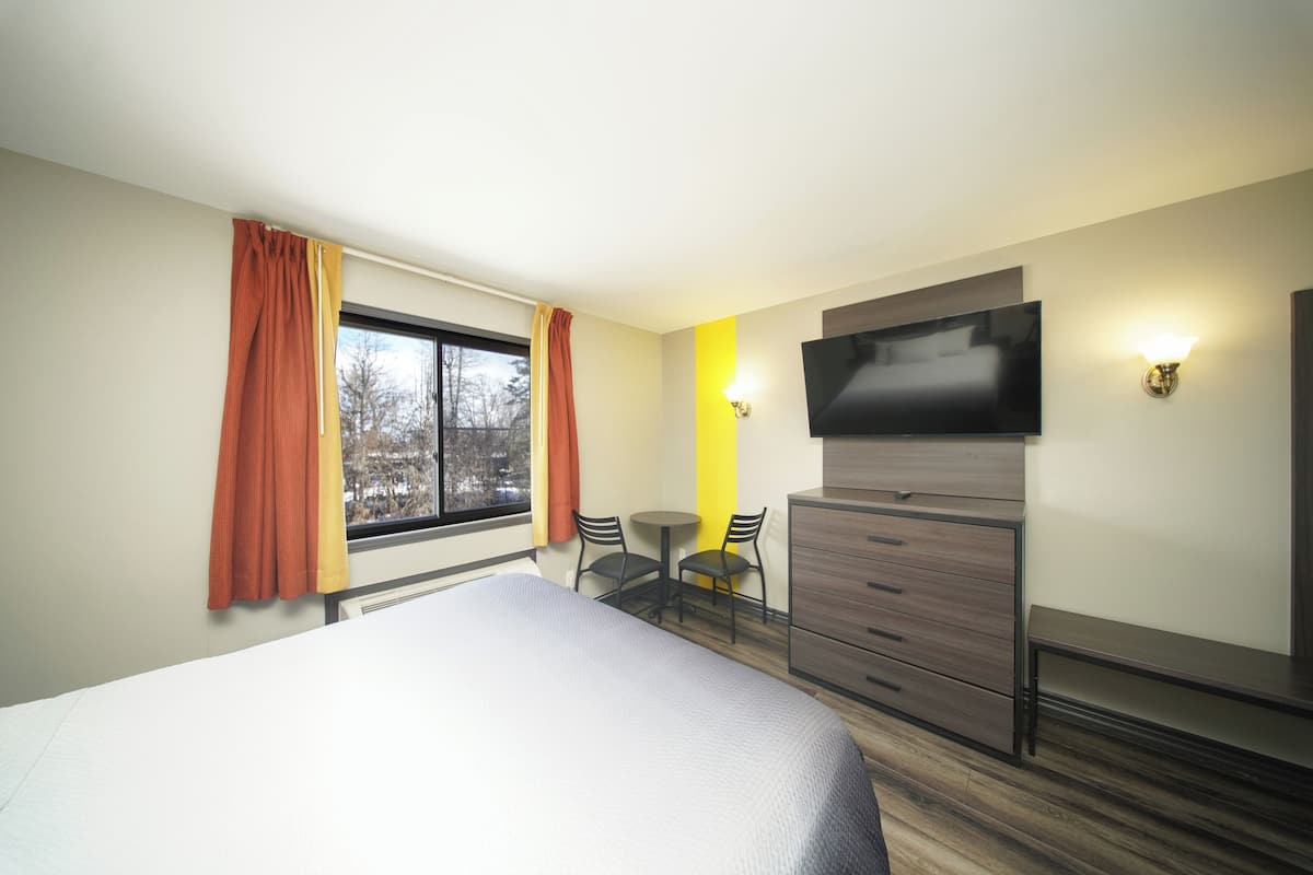 Quarto de hotel com cama, escrivaninha, duas cadeiras, televisão e cómoda.