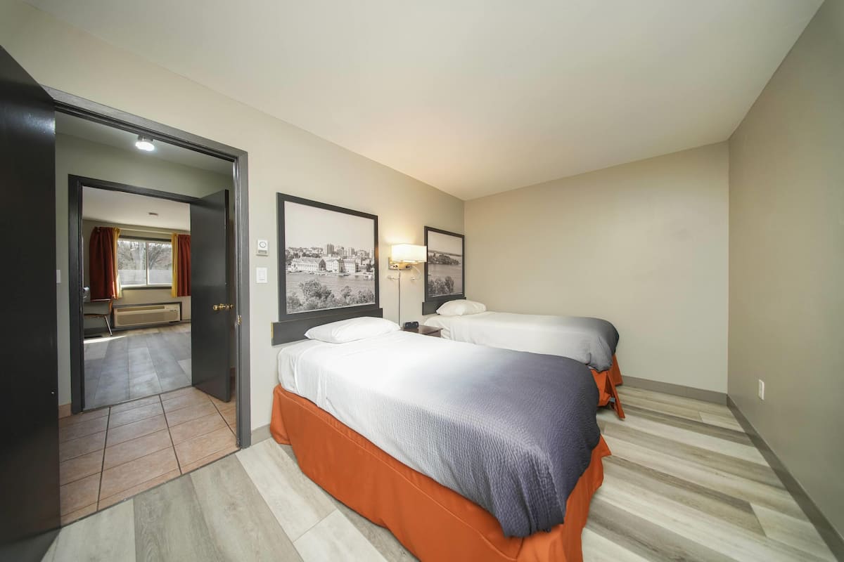 Quarto de hotel com duas camas, uma porta que dá para uma varanda e quadros nas paredes.