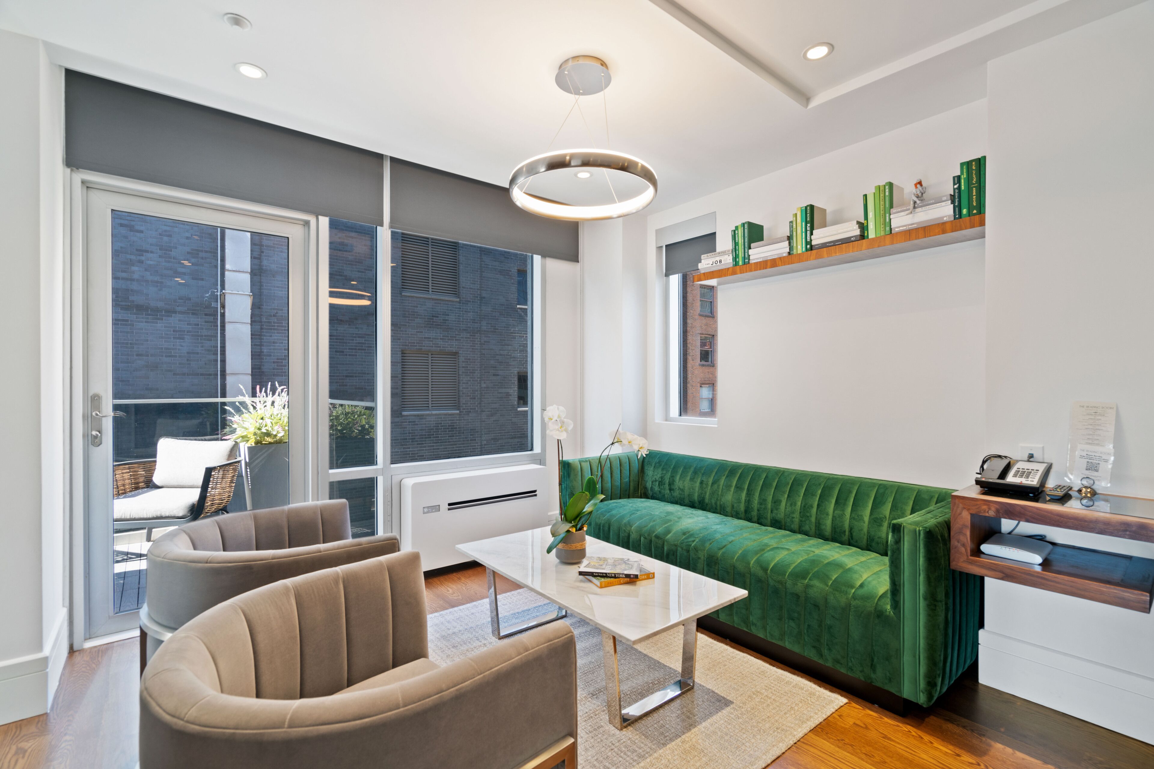 Uma sala de estar moderna com um sofá verde, duas poltronas, uma mesa de centro e uma estante com livros e objetos decorativos.