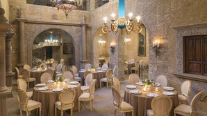 Uma sala de jantar luxuosa com mesas redondas, cadeiras elegantes e lustres elaborados.