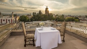Mesa posta para dois em terraço com vista para a cidade, incluindo uma torre de igreja imponente, sob um céu nublado.