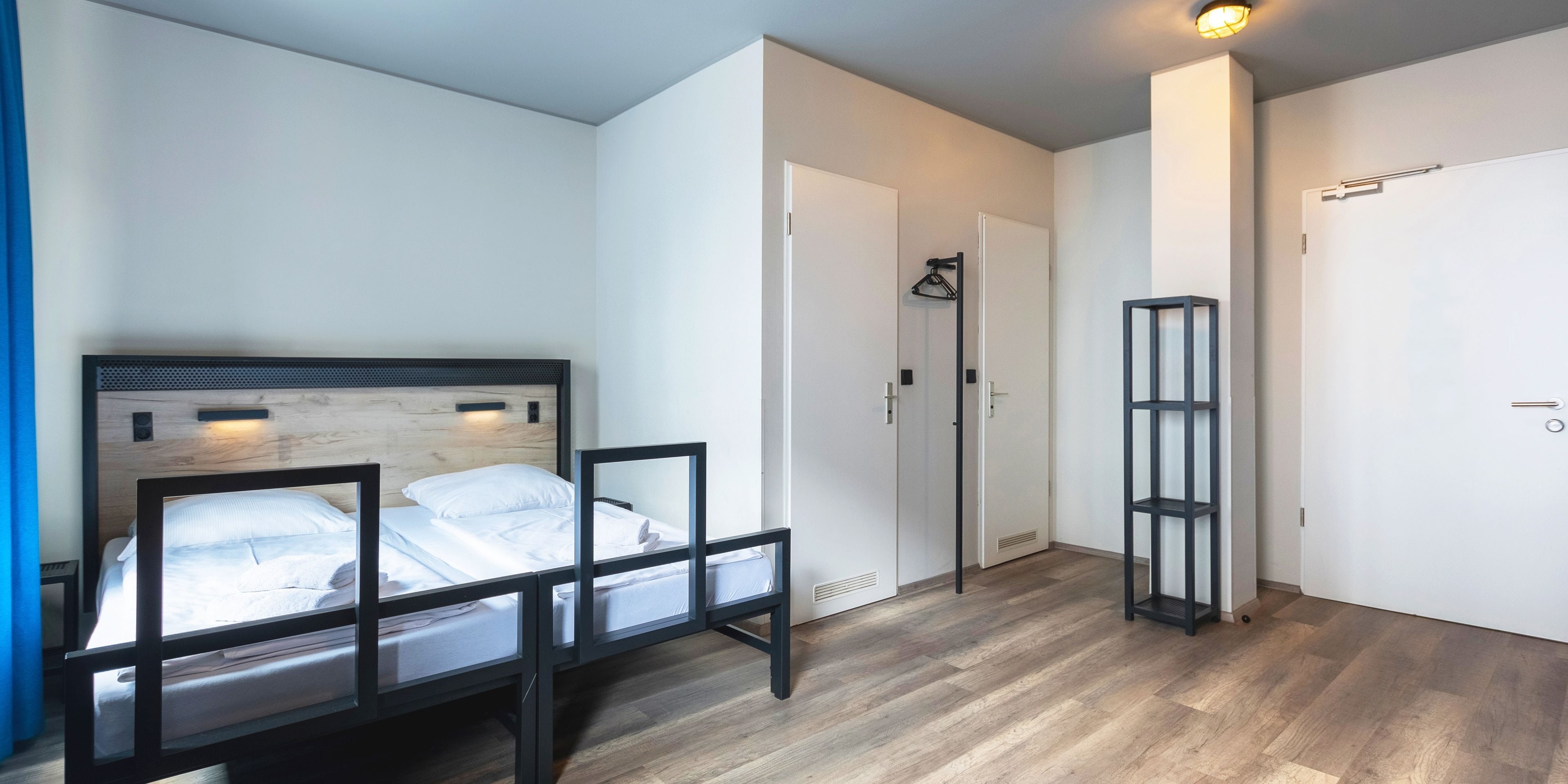 Quarto moderno com cama de madeira e cabeceira, roupa de cama branca, guarda-roupa com espelho e uma estante preta.