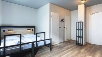 Quarto moderno com cama de madeira e cabeceira, roupa de cama branca, guarda-roupa com espelho e uma estante preta.