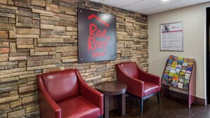 Área de recepção do Red Roof Inn, com parede de pedra, duas poltronas de couro vermelho, uma mesa pequena e um mural com diversos folhetos.