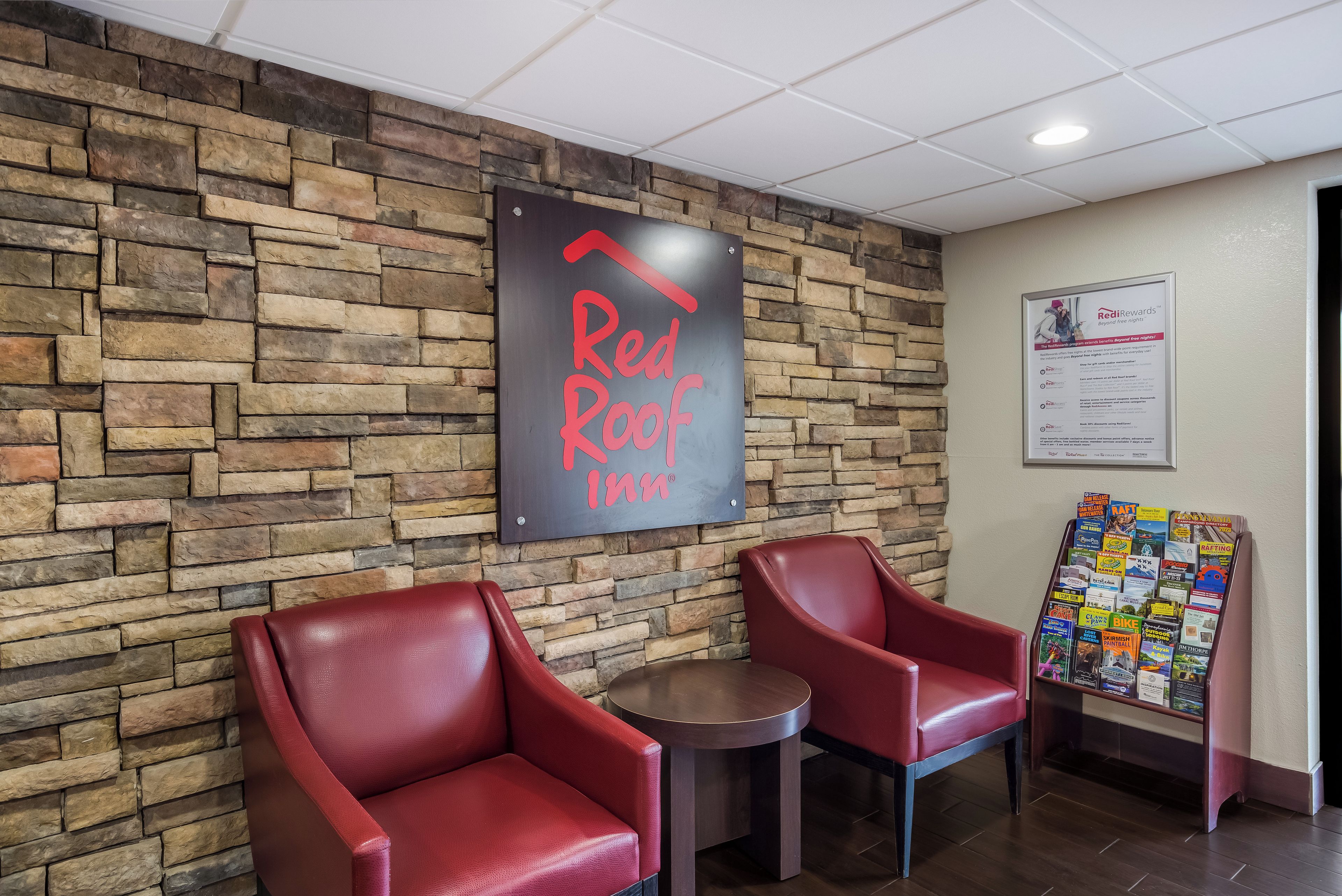 Placa da Red Roof Inn, duas poltronas de couro, uma mesinha e um mural de avisos.