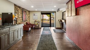 Um saguão de hotel com uma mesa de recepção, uma placa da Red Roof Inn e uma placa indicando 'Wi-Fi Gratuito em Todas as Quartas'.