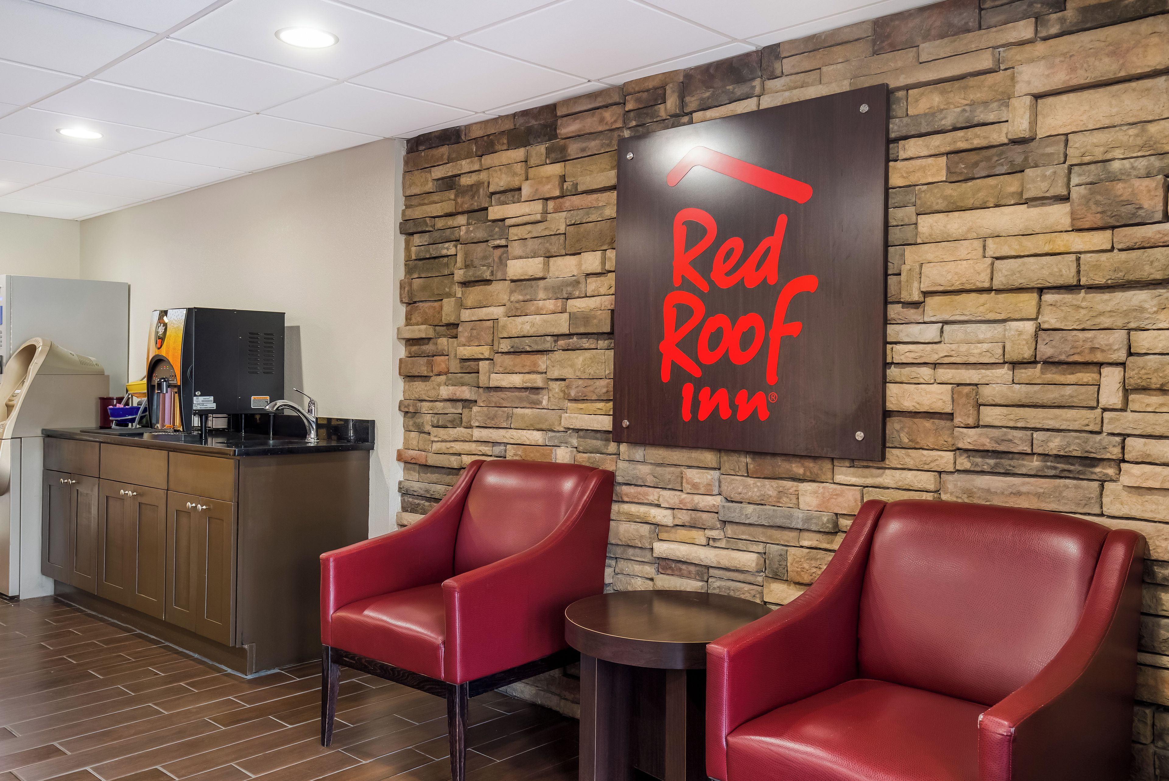 Área de recepção do Red Roof Inn com parede de pedra ao fundo, uma máquina de café e duas poltronas de couro.