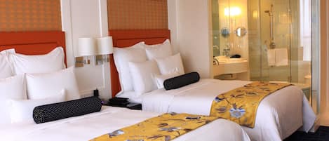 Quarto de hotel com duas camas, banheiro com chuveiro de vidro e um lustre.