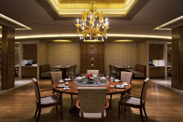 Uma sala de jantar formal com um grande candelabro, mesa redonda e várias cadeiras.